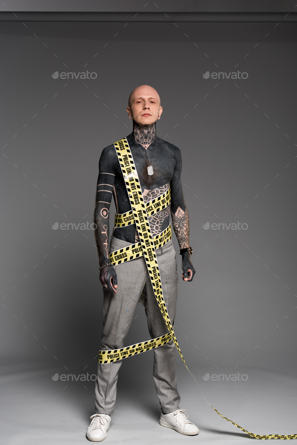 full length view of bald shirtless tattooed man with police line around ...