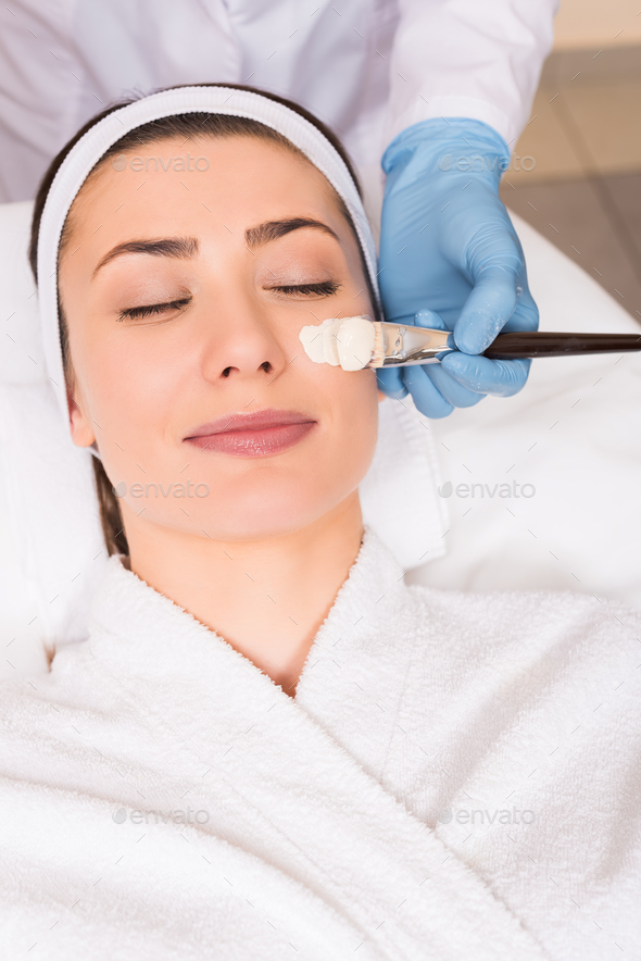 beautician beginning to apply cosmetic mask on woman face with cosmetic ...