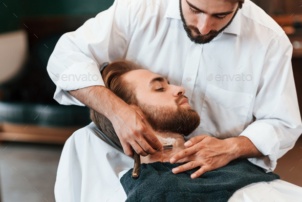 On the neck, shaving the beard. Man is visiting modern barber shop ...