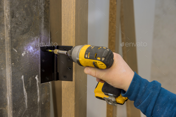 Close-up carpenter process of hands screwing hinge on a door with ...