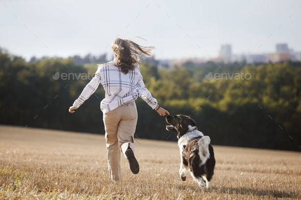 Happy teen girl with her dog running across field Stock Photo by Chalabala