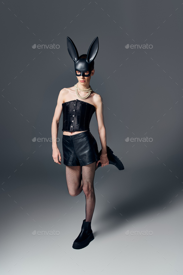 androgynous model in corset posing in bdsm bunny mask on grey, queer ...