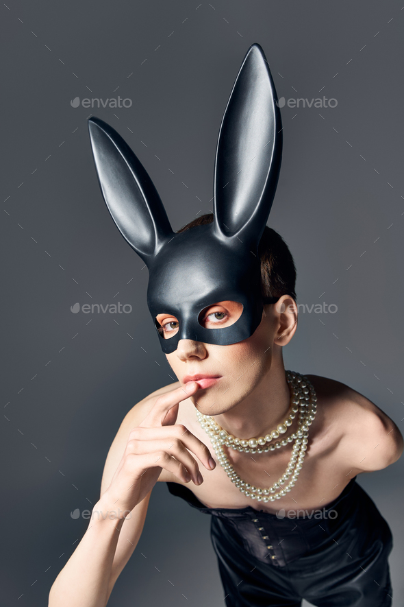 queer person in corset and bdsm bunny mask posing on grey, finger near ...