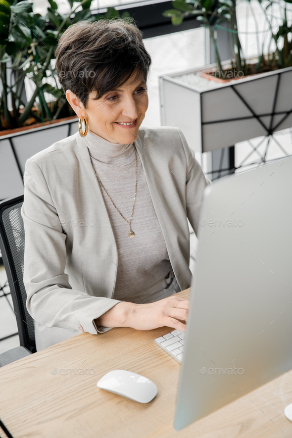 positive and stylish middle aged corporate manager working on computer ...