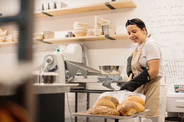 Female baker using a peel to take out a loaf of bread of the oven in a ...