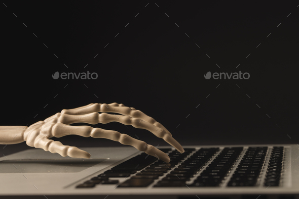Plastic skeleton hand on laptop keyboard with copy space on black ...