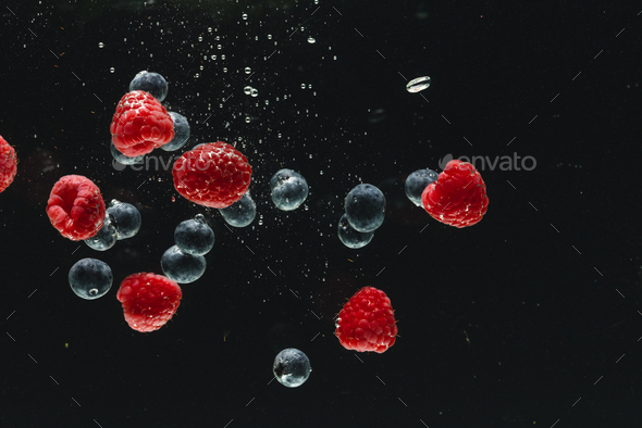 Close up of fresh berries falling into water with copy space on black ...