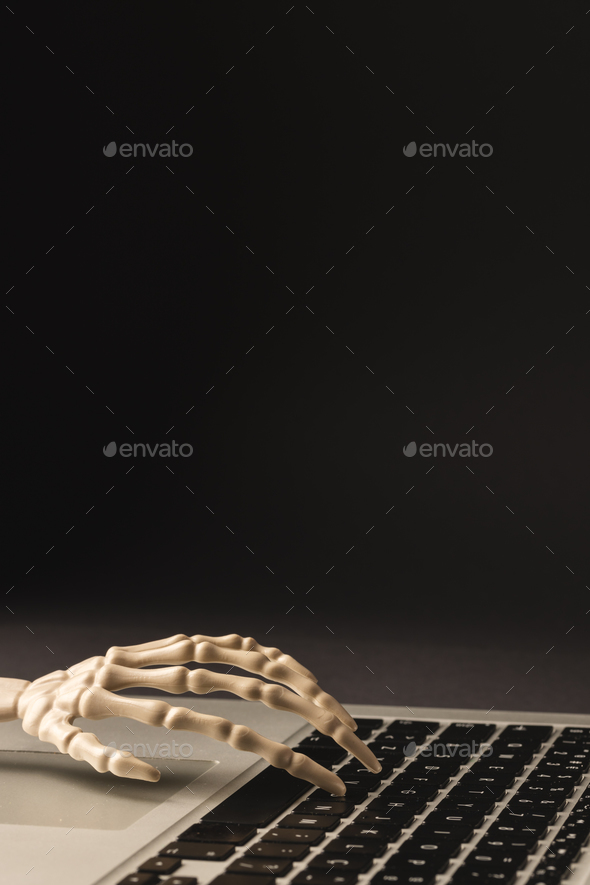 Vertical image of plastic skeleton hand on laptop keyboard with copy ...