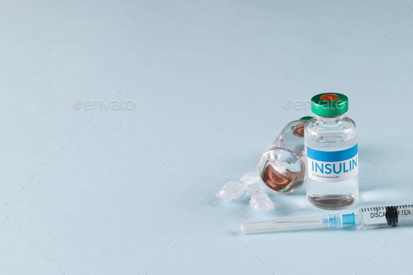 Vials of insulin with caplets and syringe on blue background with copy ...