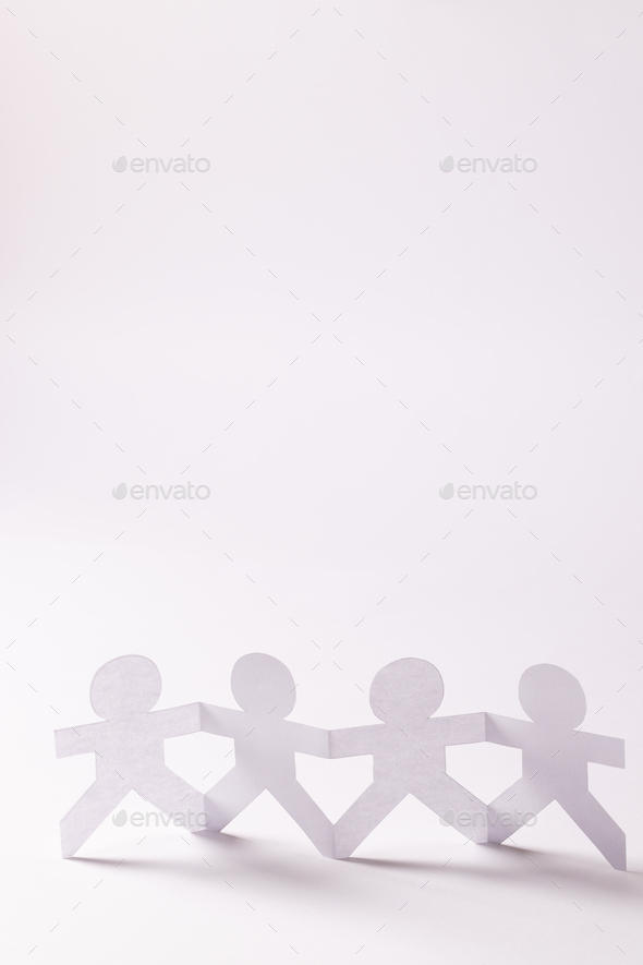 Close up of four paper cut out people figures holding hands with copy space on white background ...
