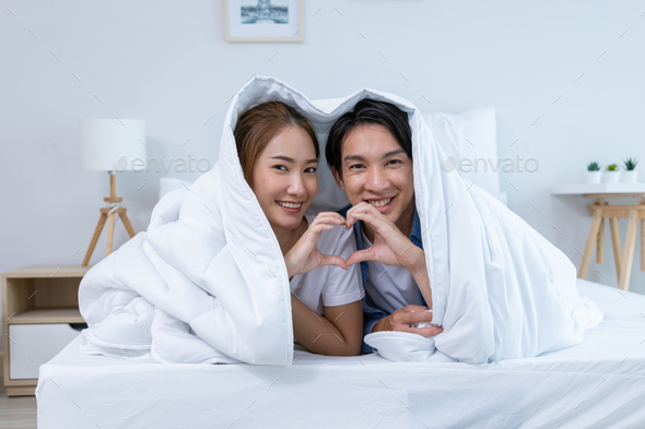 Couple playing in bed at home, hugging soft pillow, nose touching ...