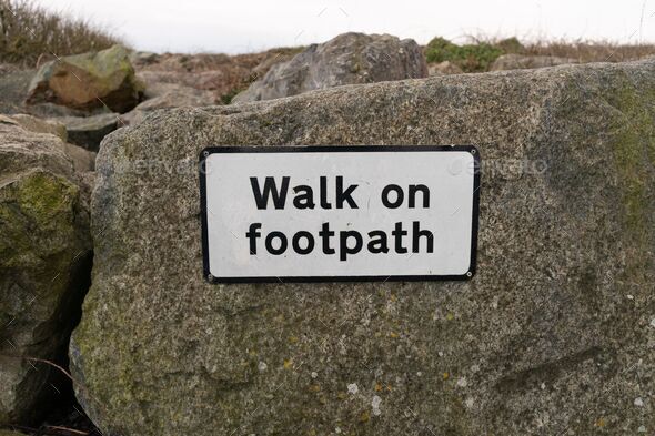 Close-up of a stone wall with a white sign reading 'Walk on Footpath ...