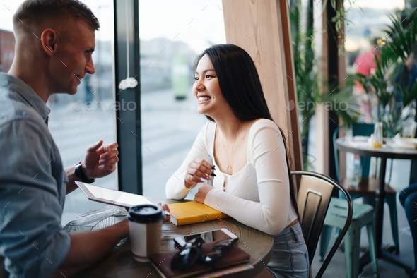 Cheerful male and female best friends laughing at cafeteria table ...