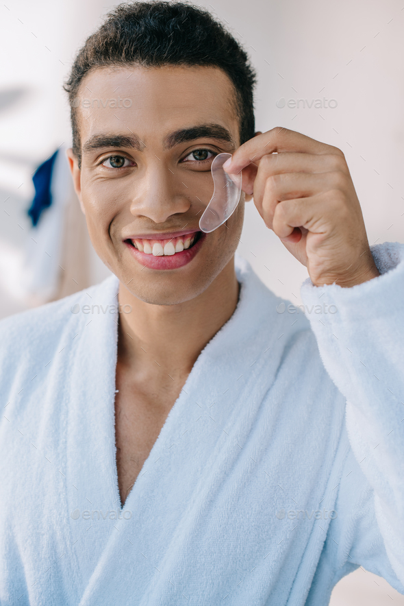 handsome young man in bathrobe showing patch and smiling while looking ...