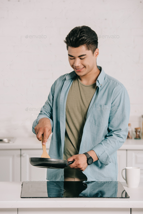 smiling asian man cooking breakfast on frying pan in kitchen Stock ...