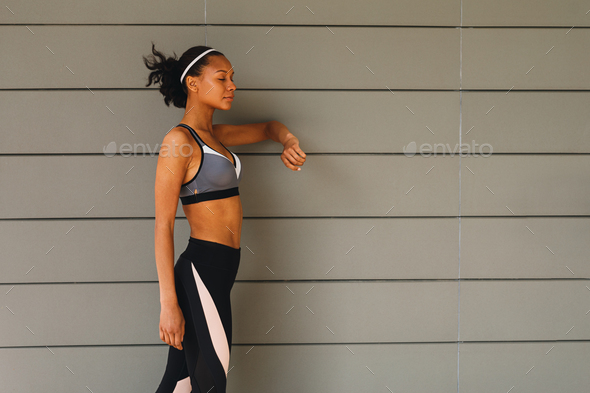 Side view of a slim female athlete taking a break, leaning hand on wall ...