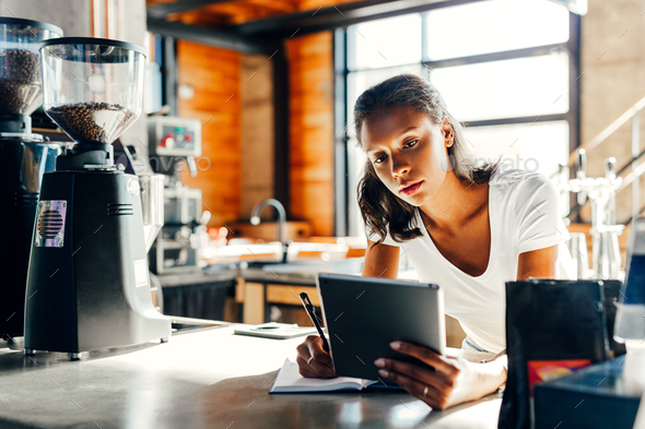 Cafe owner leaning on counter making notes in cafe Stock Photo by ...