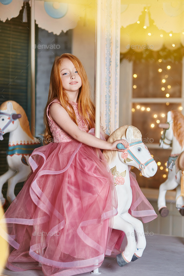 Beautiful red-haired girl with long hair and blue eyes rides carousel ...