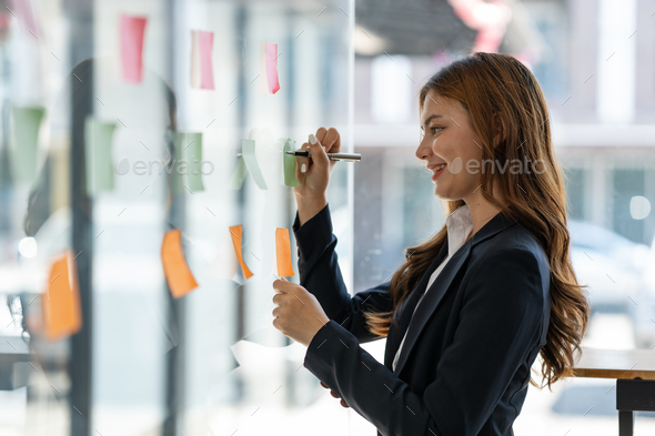 Happy asian businesswoman working with sticky notes on glass wall as ...