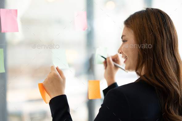 Happy asian businesswoman working with sticky notes on glass wall as ...