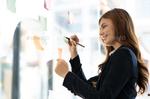 Happy asian businesswoman working with sticky notes on glass wall as ...