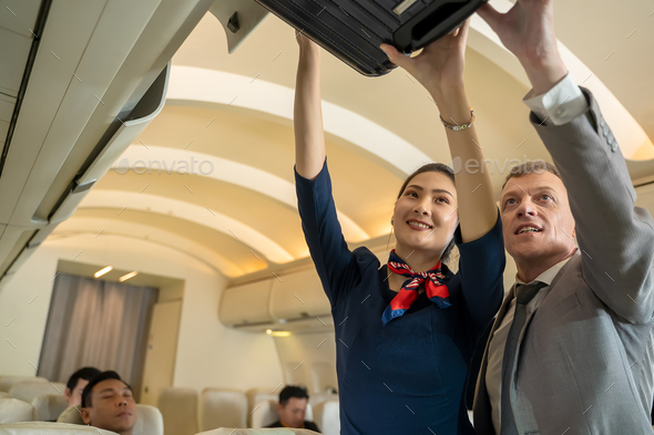 Friendly flight attendant helping passenger to put luggage on the top ...