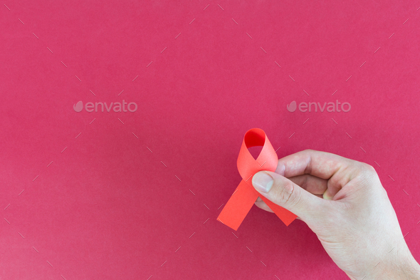 Human hand holding World AIDs day red ribbon symbol on the red background Stock Photo by wirestock