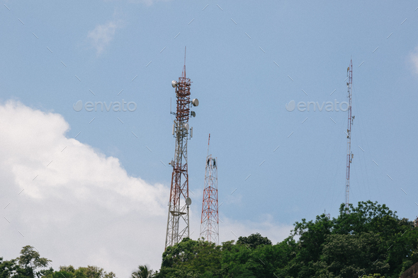 Closeup shot of a telecommunication tower among trees with a blue sky ...