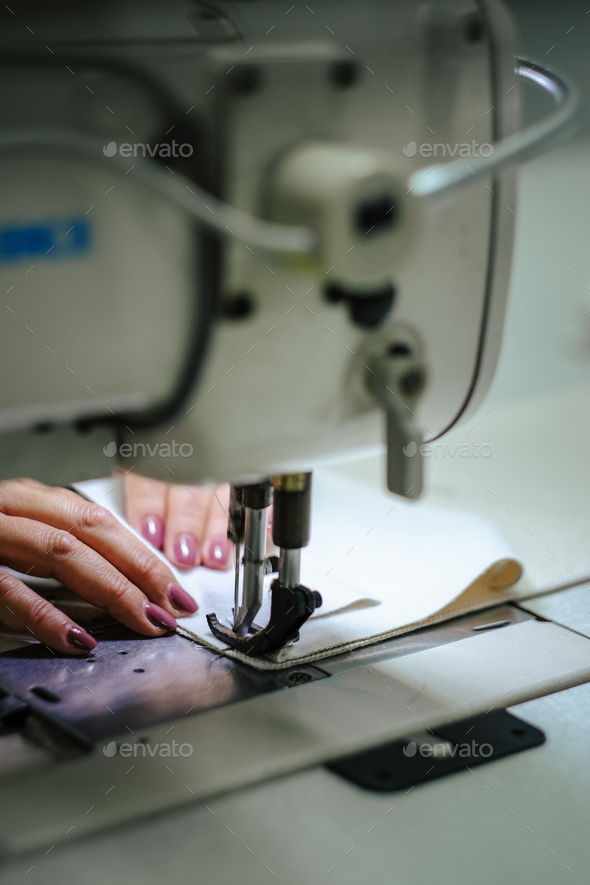 Vertical closeup shot of female hands operating an industrial sewing ...