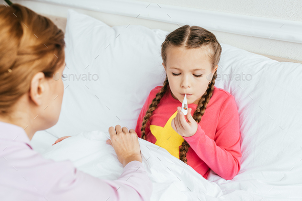 diseased daughter measuring fever with thermometer while sitting in bed with mom Stock Photo by ...