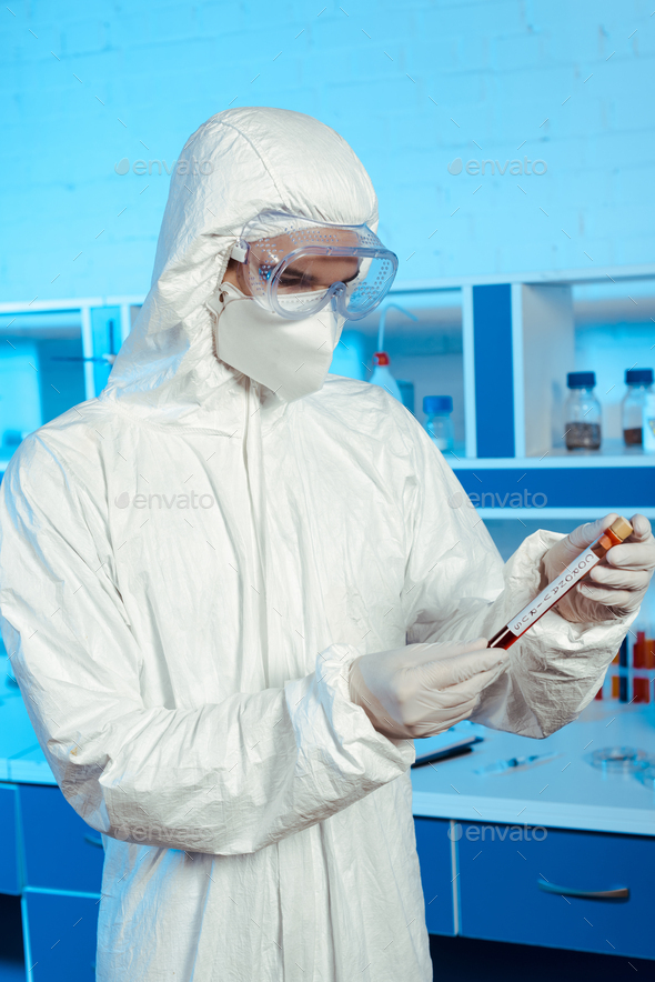 scientist in hazmat suit and goggles holding test tube with coronavirus ...