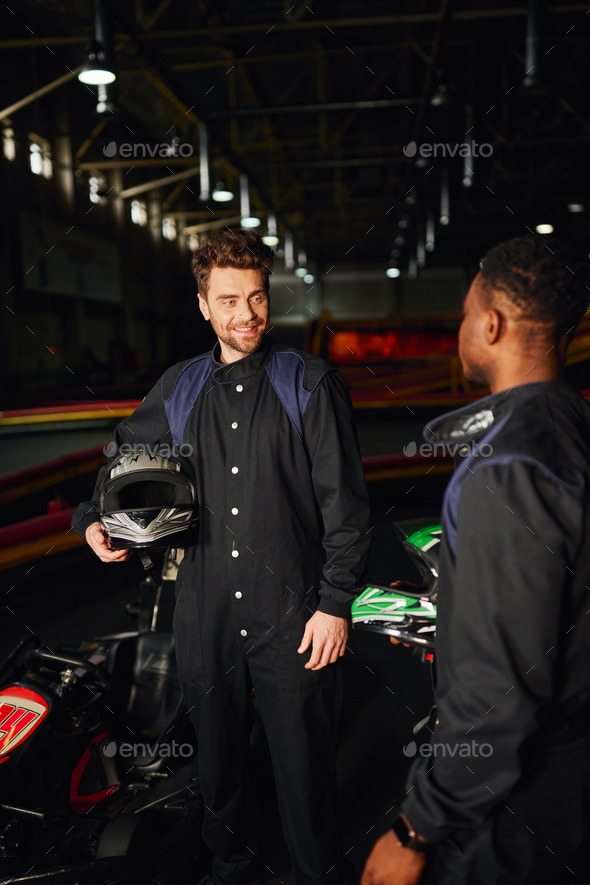 cheerful kart driver holding helmet and looking at african american ...