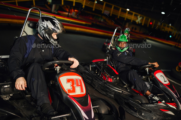 multiethnic competitors driving go kart on indoor circuit, speed racing ...