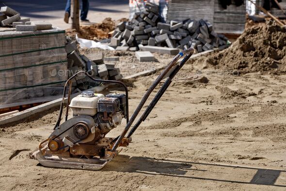 Old gasoline compactor on sandy soil against a stack of paving slabs on ...