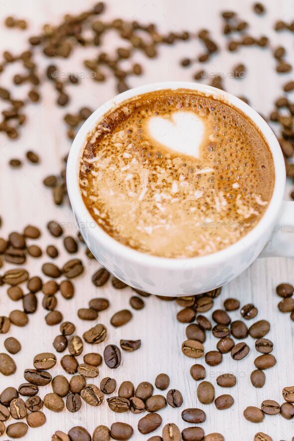 Vertical, top view of a cup of coffee with a heart foam surrounded by ...
