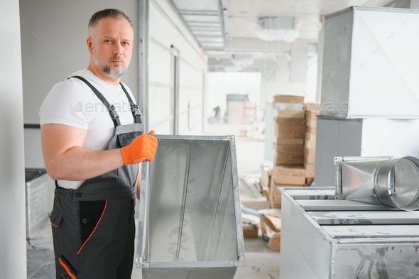 Man setting up ventilation system indoors. A male worker installs air ...