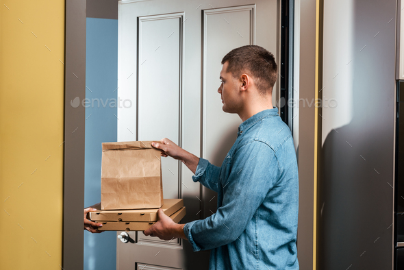 delivery man giving package to young man near open door at home Stock ...