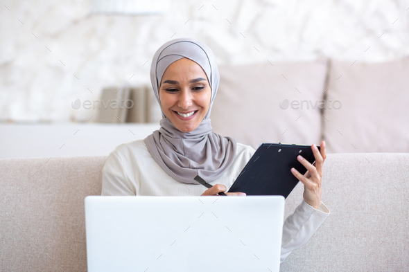 Close-up photo of a young Muslim woman in a hijab working from home on ...