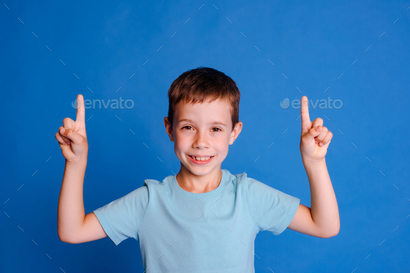 headshot boy point index fingers up to free copy space on light blue ...