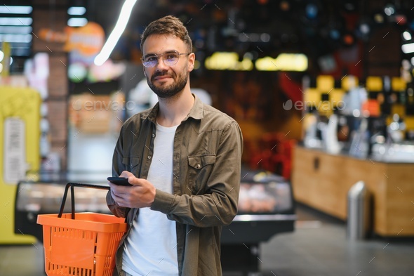 Handsome man shopping in supermarket, smilling, using phone. Stock ...