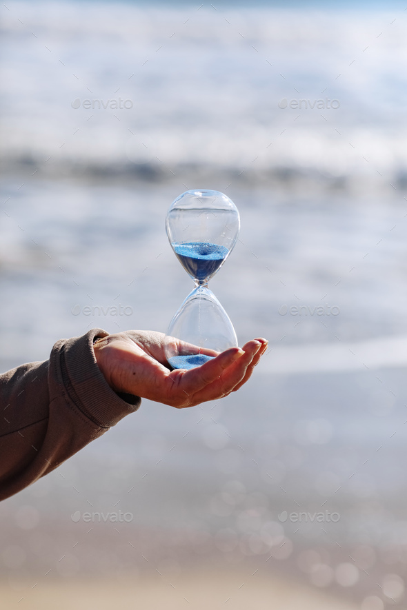 Time is running fast. Hourglass with blue sand inside in mature woman's ...