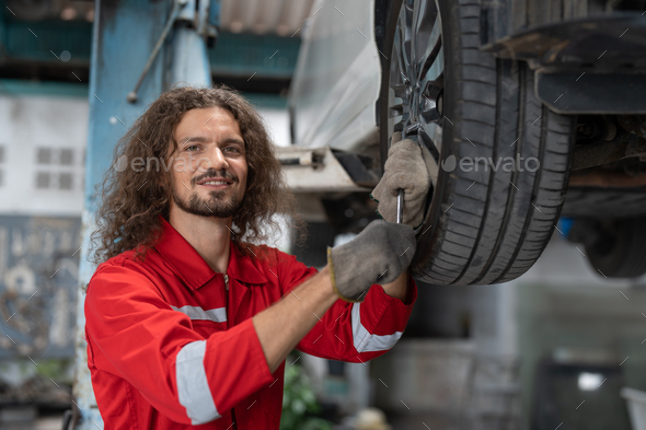 Smiling car mechanic man using spanner to changing car wheel, disc ...