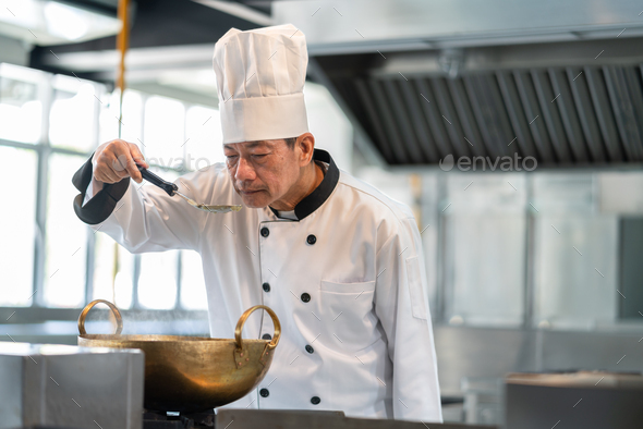 Professional senior Asian chef man in white dress tasting delicious ...