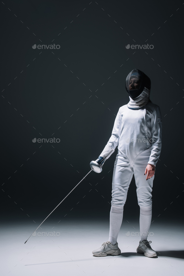 Fencer in fencing mask holding rapier while standing on white surface ...
