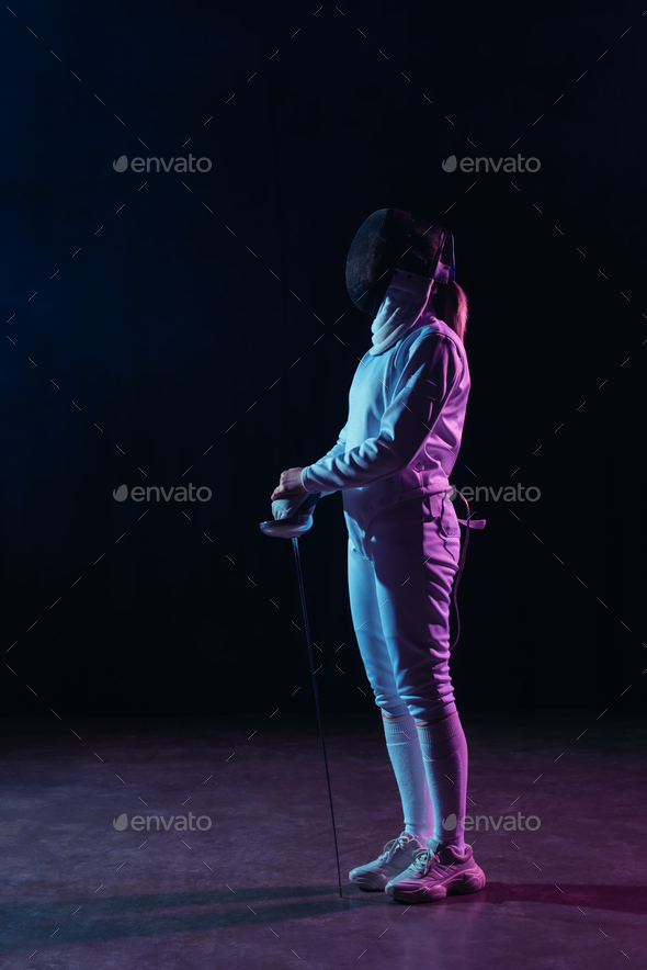 Side view of fencer holding rapier on black background with lighting ...