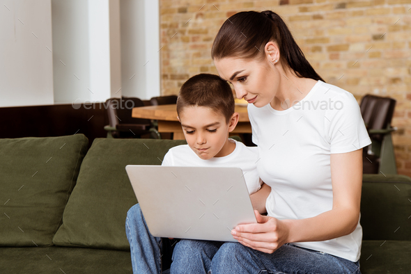 Mother and son using laptop on couch at home Stock Photo by LightFieldStudios