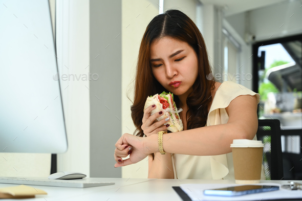 Busy asian female worker eating sandwich and checking time on watch ...