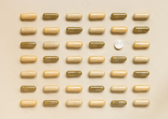 Mix of medical capsules with onewhite pill in lines on light beige top ...