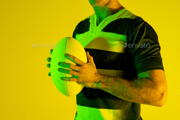 Caucasian male rugby player with rugby ball over orange lighting Stock ...
