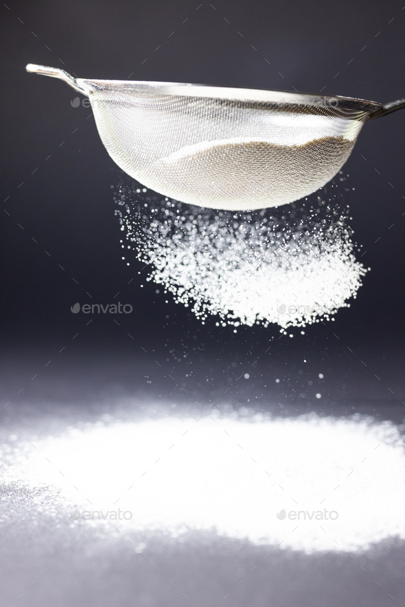 Close-up of flour sifting by sieve on table against black background ...